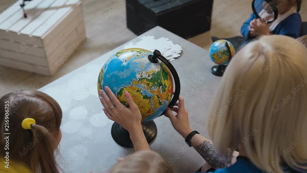 Top view. A stylish teacher with a tattoo shows the kids a globe ...