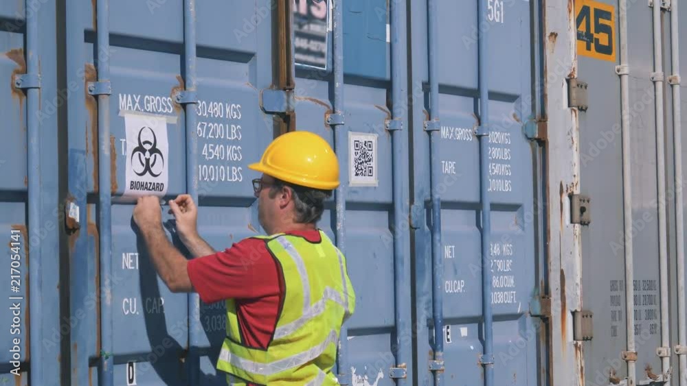 Shipping worker sticking a biohazard sign on a shipping container in a ...