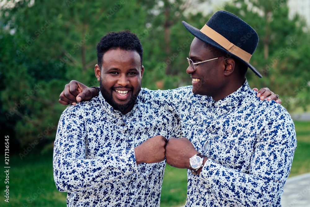 two black men in stylish suits meeting in a summer park. African ...