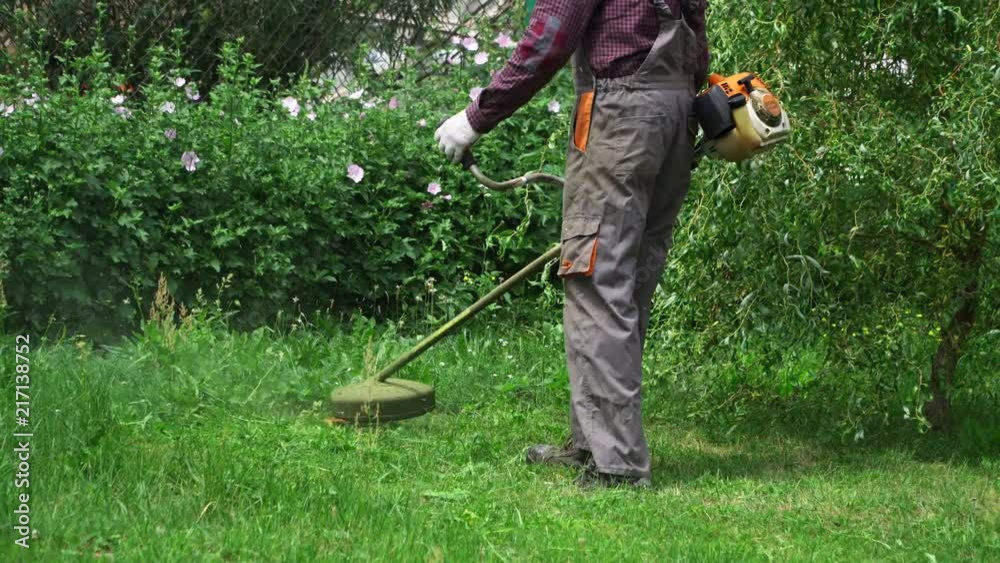 Brushcutter machine slashing grass weeds in a pattern, opearted by a ...
