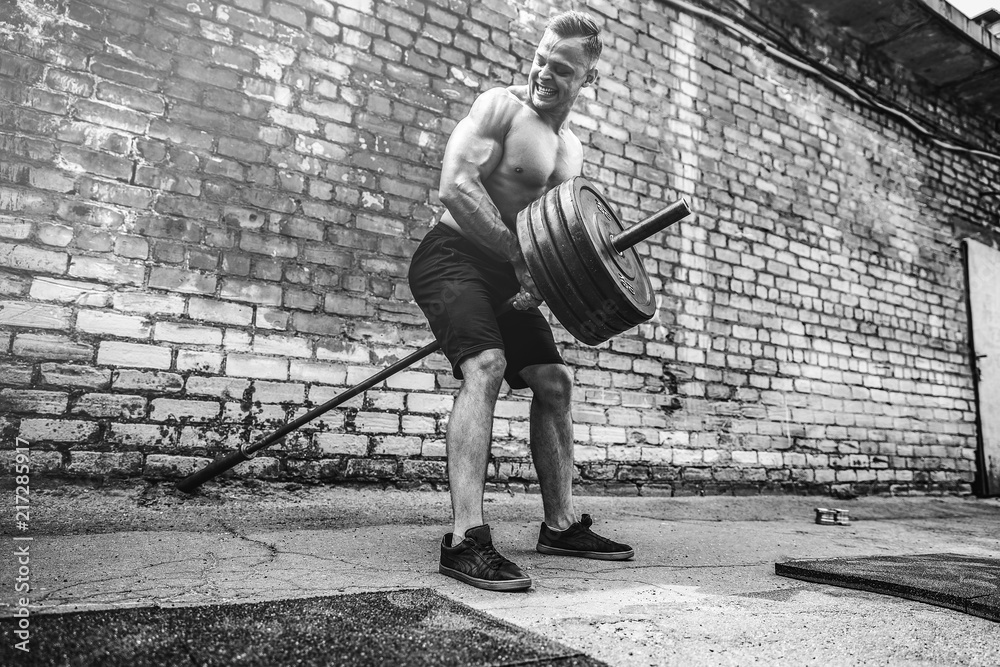 Athletic man working out with a barbell in front of brick wall ...