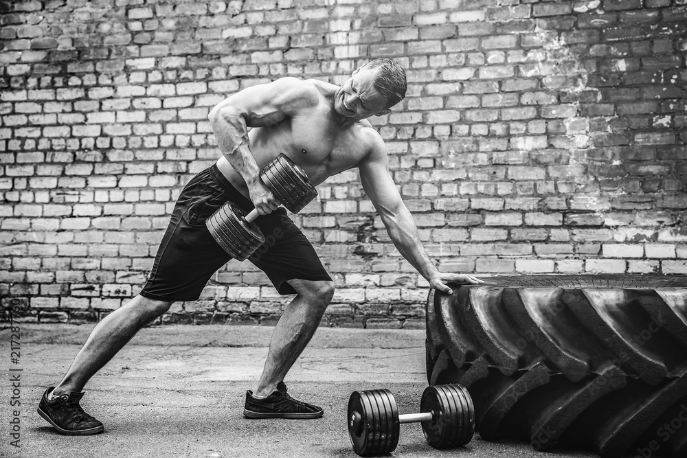 Athletic man working out with a dumbbell in front of brick wall ...