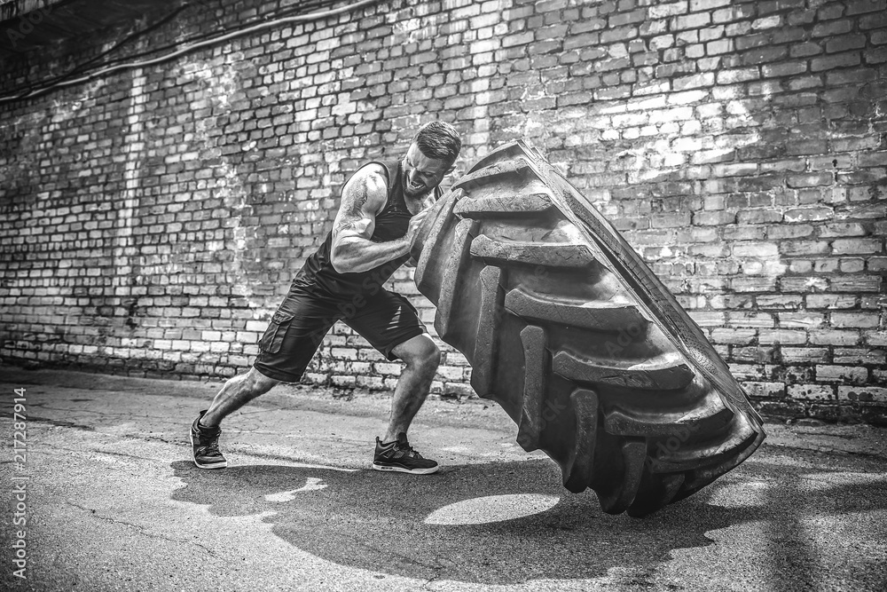 Muscular bearded tattooed fitness shirtless man moving large tire in ...