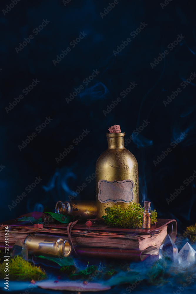 Golden potion bottle in a still life with an occult equipment on a dark ...