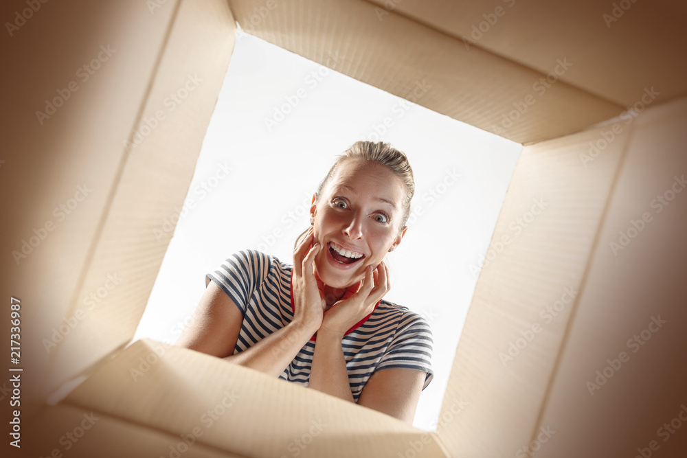The surprised woman unpacking, opening carton box and looking inside ...