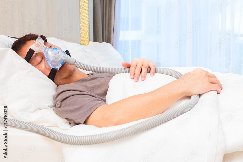 Asian man wearing CPAP mask, connecting to air hose, sleeping on his ...