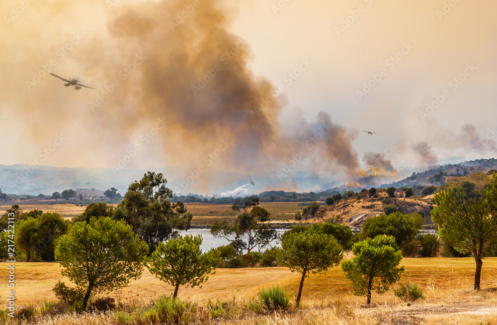 Water bomber planes tackle a fire along the side of a river. There is a ...