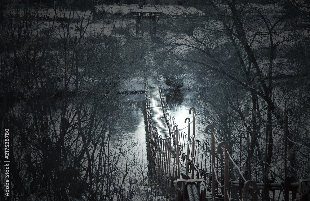 Creepy dark old suspension bridge across the river in the fog ...