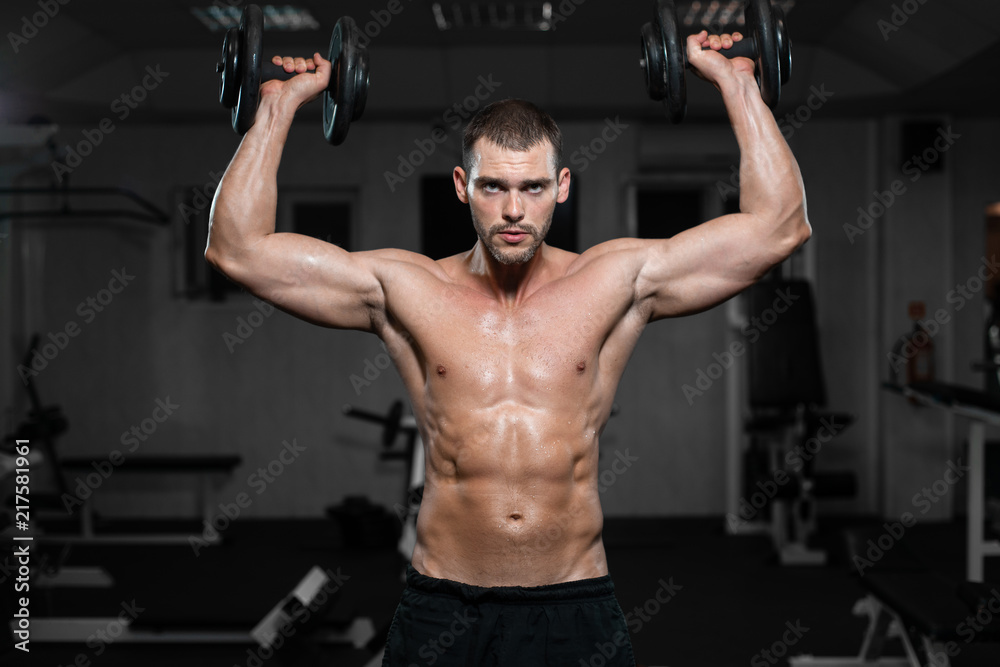 Muscular man in the gym training with dumbbells, guy pumps his deltoid ...