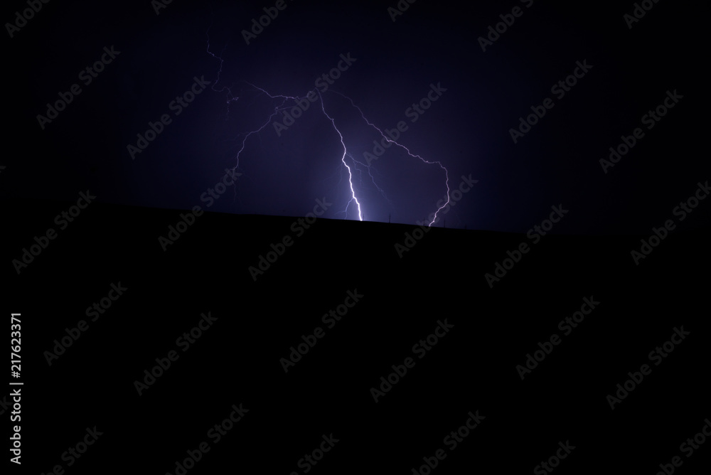 Single lightning strike in nature in a field with colours of white and ...