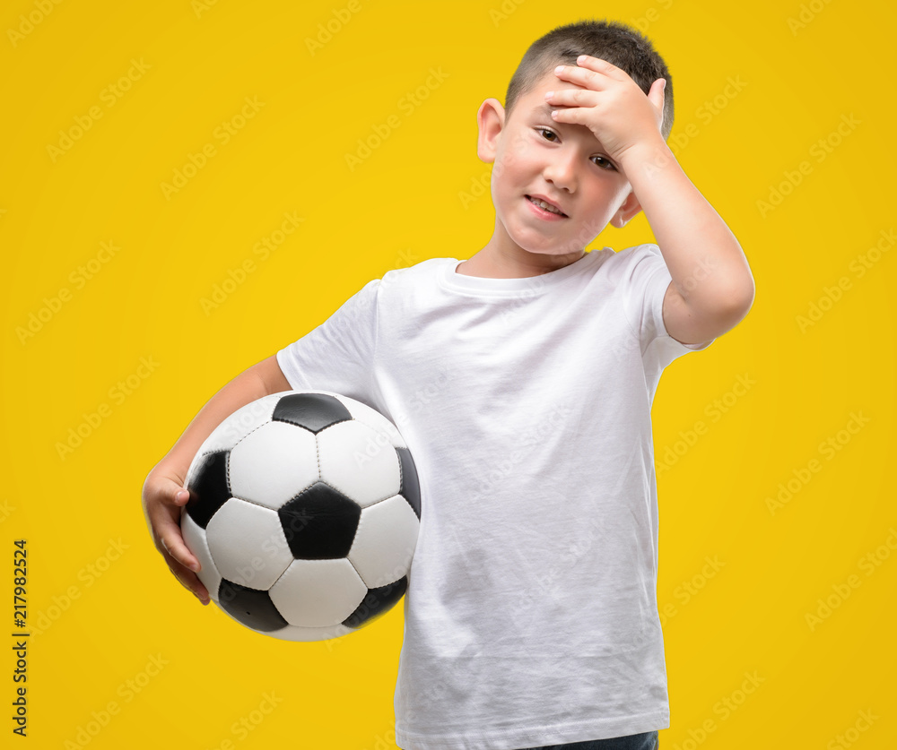 Dark haired little child playing with soccer ball stressed with hand on ...