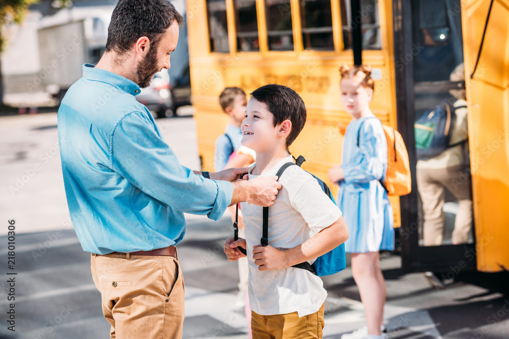 handsome father talking to his son before school in front of school bus ...