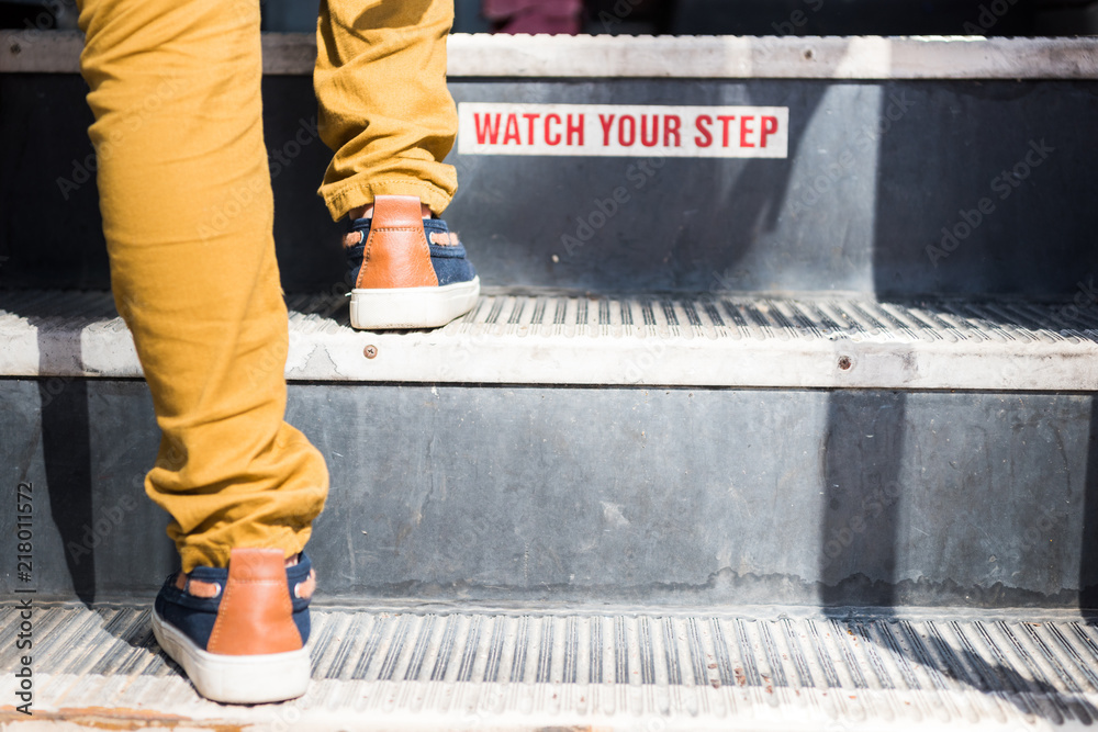 cropped shot of child going upstairs in bus with "watch your step" sign ...