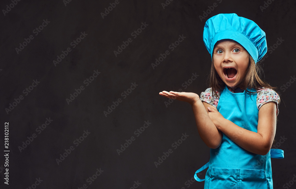 Surprised little girl dressed in blue cook posing in a studio. Isolated ...