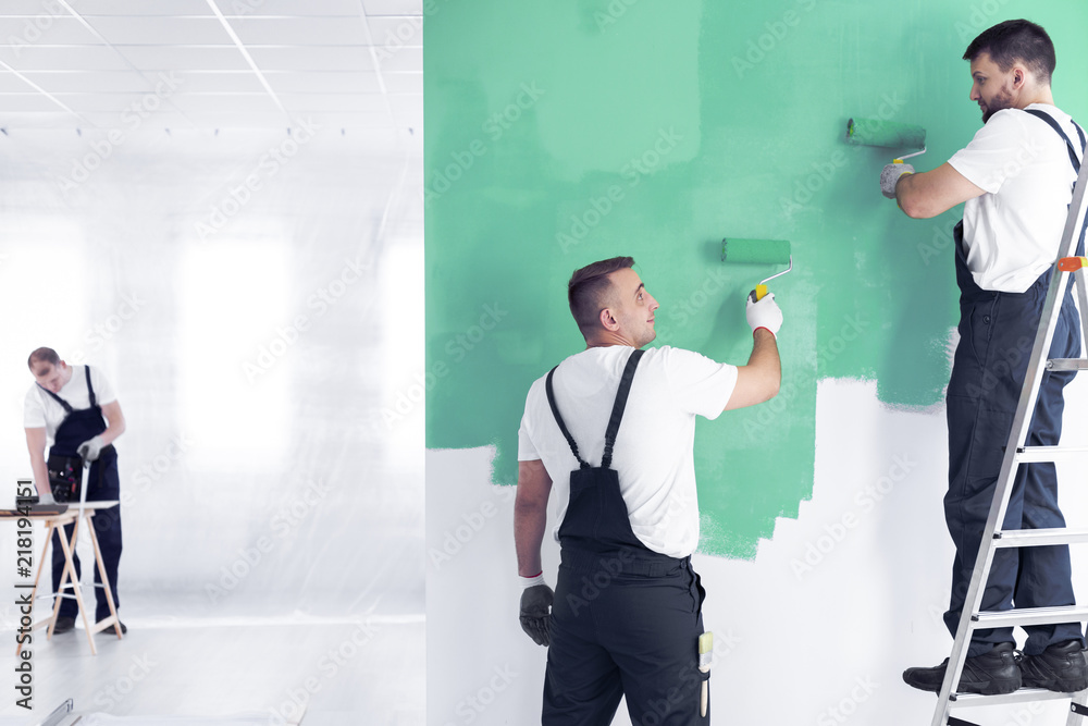 Wall painter on a ladder and a renovation crew worker painting a wall ...