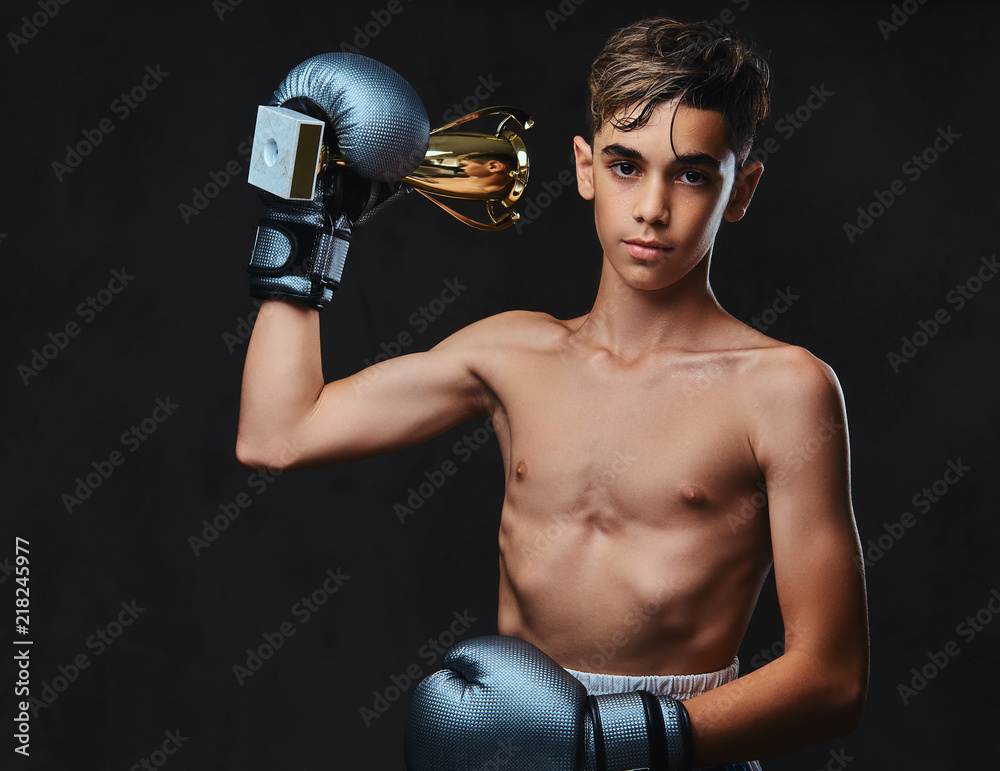 Young shirtless boxer champion wearing gloves holds a winner's cup ...