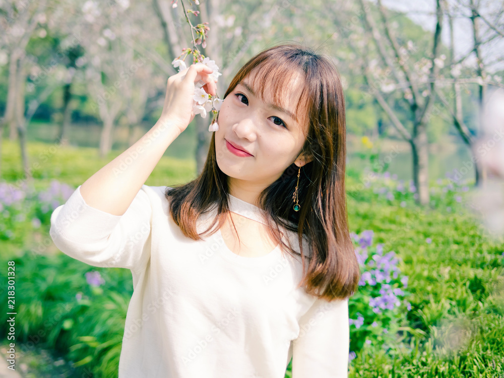 Outdoor portrait of beautiful young Chinese girl smiling among blossom ...