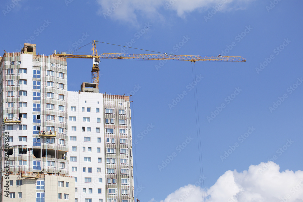 Tower building crane against the blue sky. On the wall of the building ...