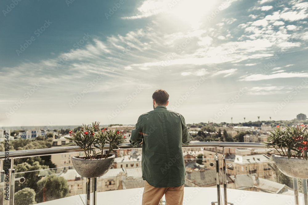 Resting. Back view of young guy leaning against balcony railing and ...