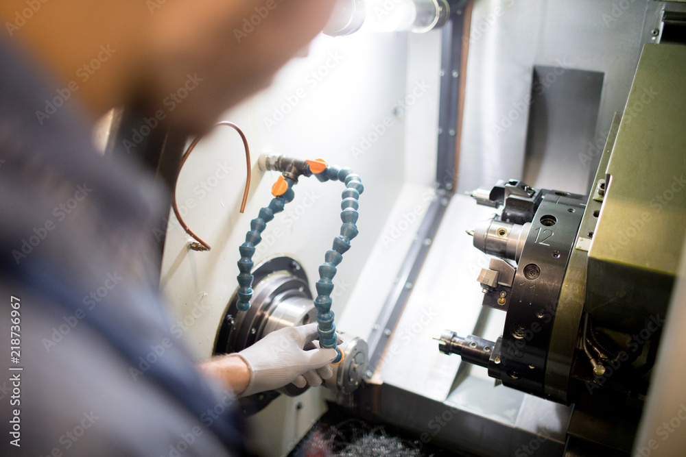 Focus on lathe machine and operator wearing safety goggles adjusting ...