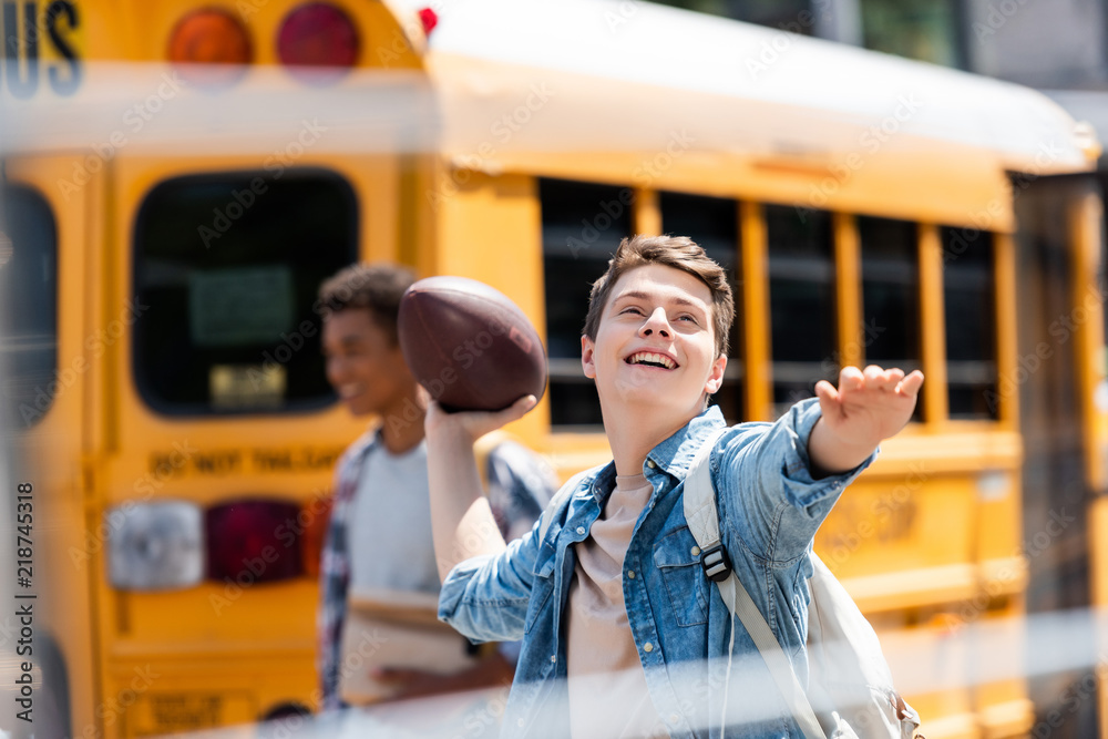 happy teen schoolboy throwing american football ball in front of school ...