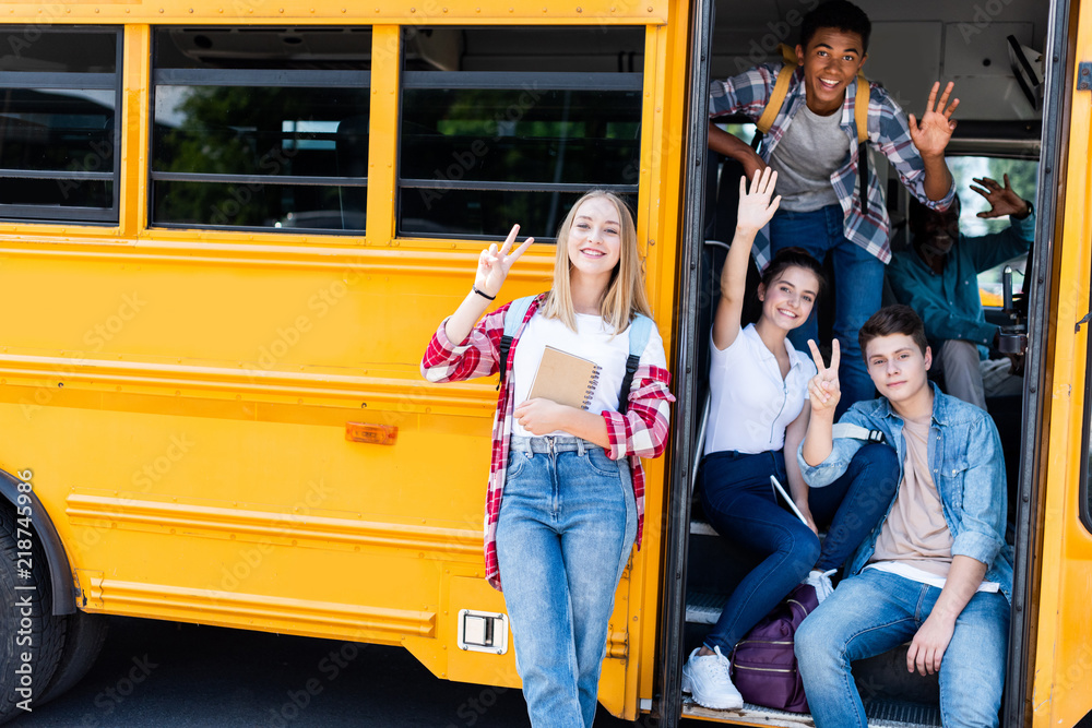 group of teen scholars sitting at school bus with driver inside and ...