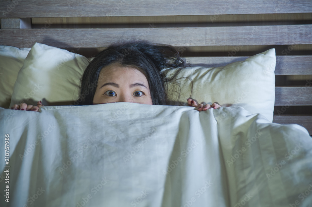 young scared and stressed Asian Chinese woman lying in bed suffering ...