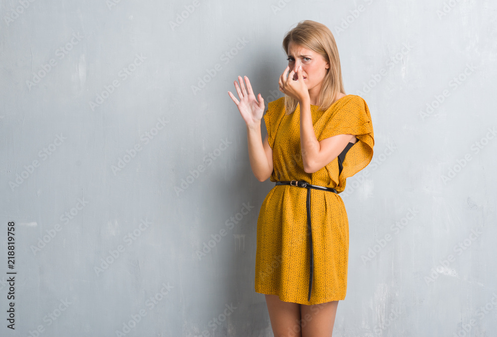 Beautiful young woman standing over grunge grey wall wearing a dress ...