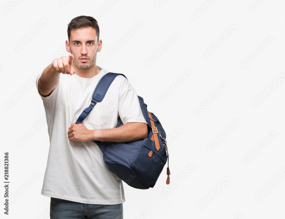 Handsome young man holding backpack pointing with finger to the camera ...