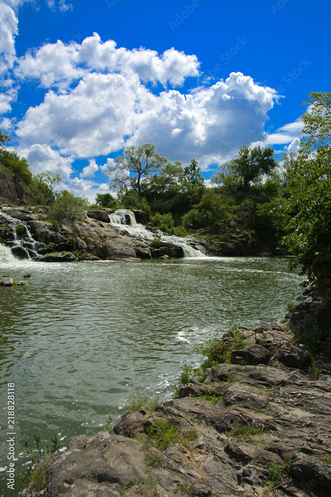 The waterfall on the river flows through and over the rocks covered ...