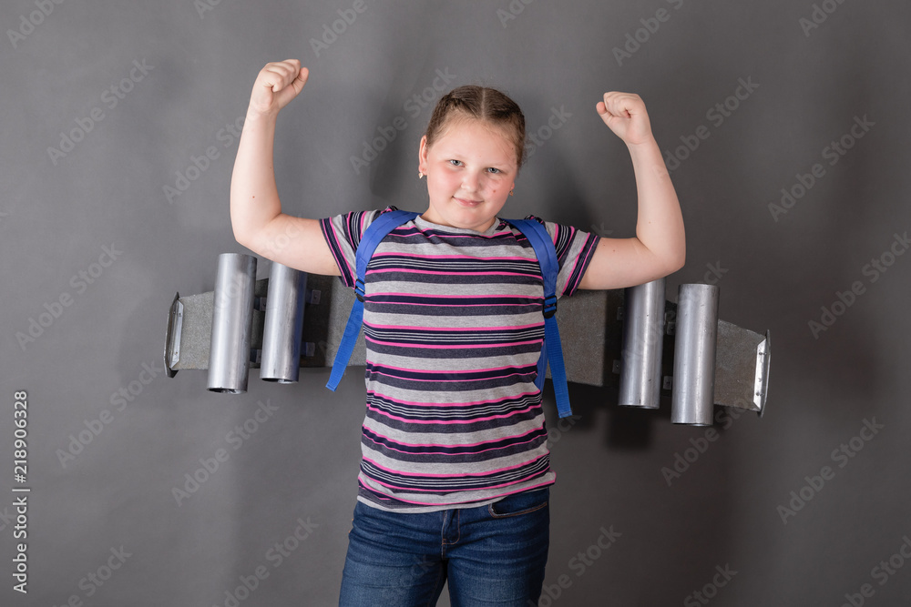 Strong stout little girl with a jetpack on his back on gray background ...