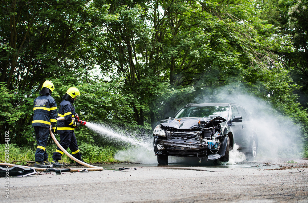 Two firefighters extinguishing a burning car after an accident. Stock ...