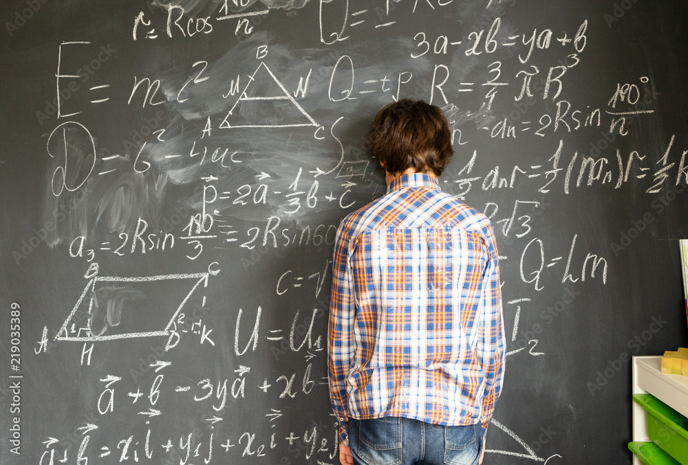 boy standing near blackboard with math formulas, school problems and ...