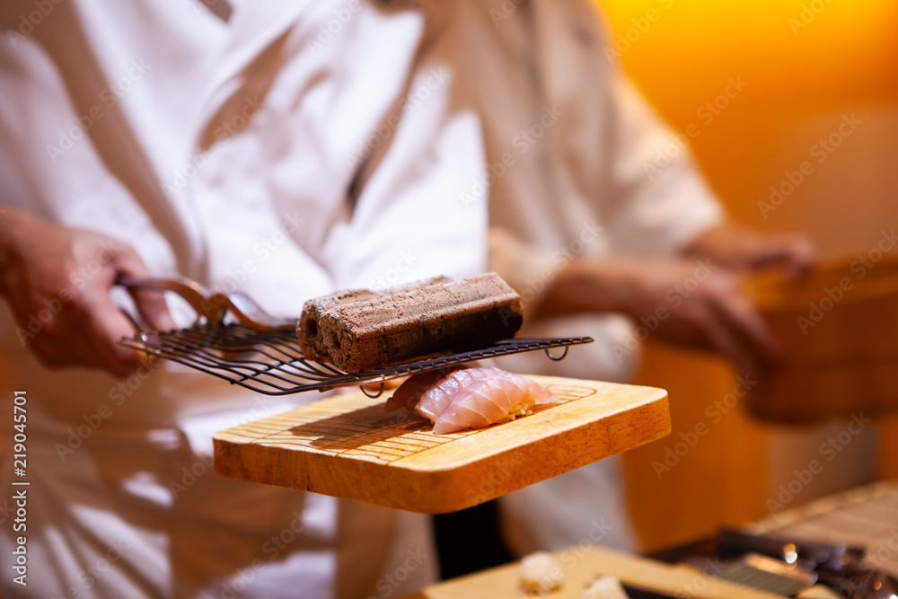 Professional sushi chef using red hot charcoal to aburi or flame seared ...