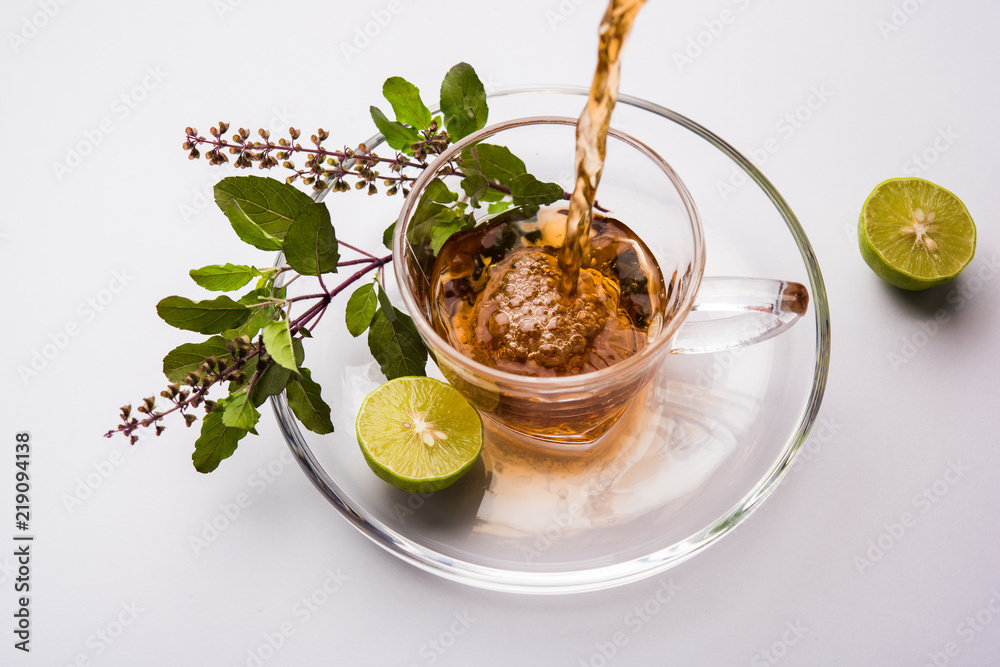 pouring Holy Basil or Tulsi Tea in transparent glass cup with saucer ...
