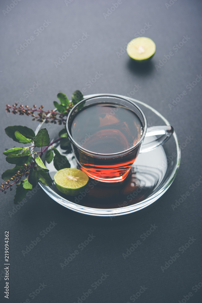 pouring Holy Basil or Tulsi Tea in transparent glass cup with saucer ...