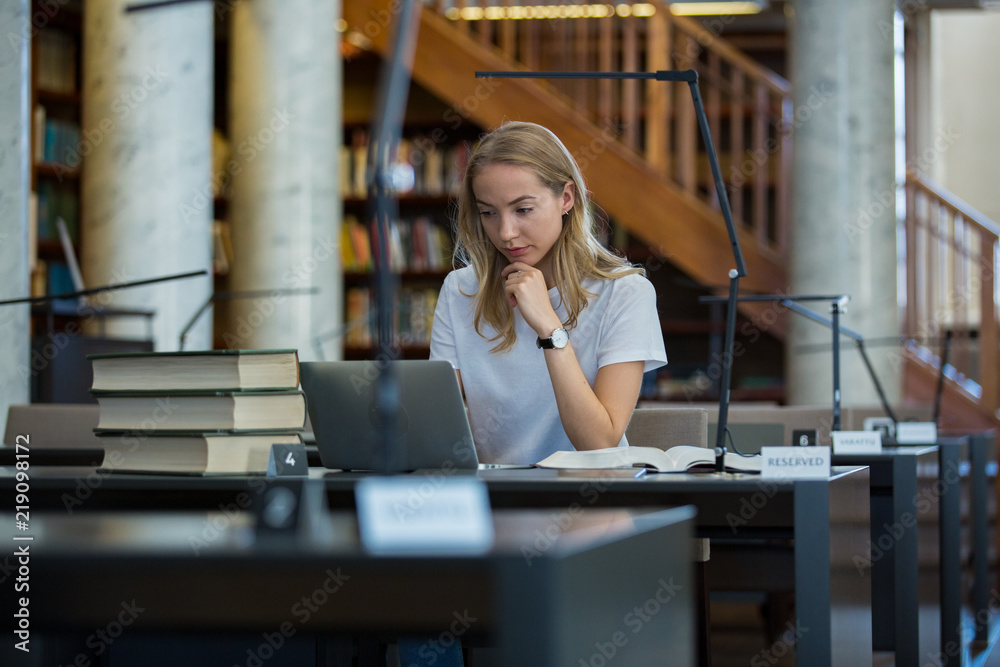 Young girl sitting at a desk in library, working at computer. Reading ...