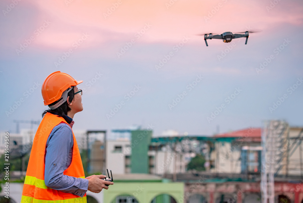 Young Asian engineer man flying drone over construction site during ...