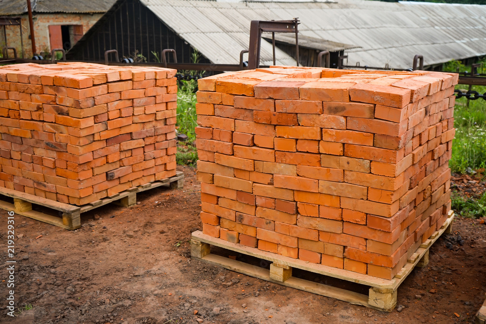 Red clay bricks are stacked on wooden pallets. Production of bricks ...