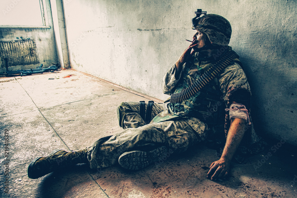 Soldier in combat uniform and ammo belt over chest, sitting on floor ...