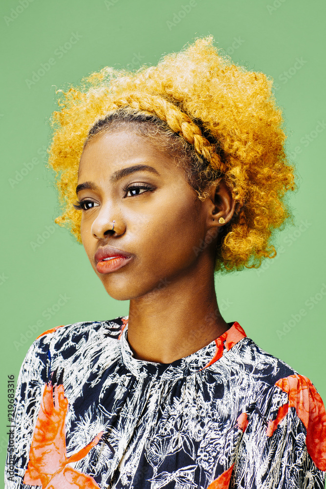 Young girl with bleached curly hair looking off camera, in front of a ...