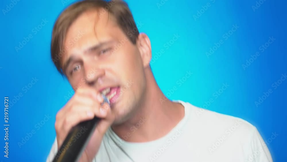 a crazy funny young man sings songs into a microphone. color background ...