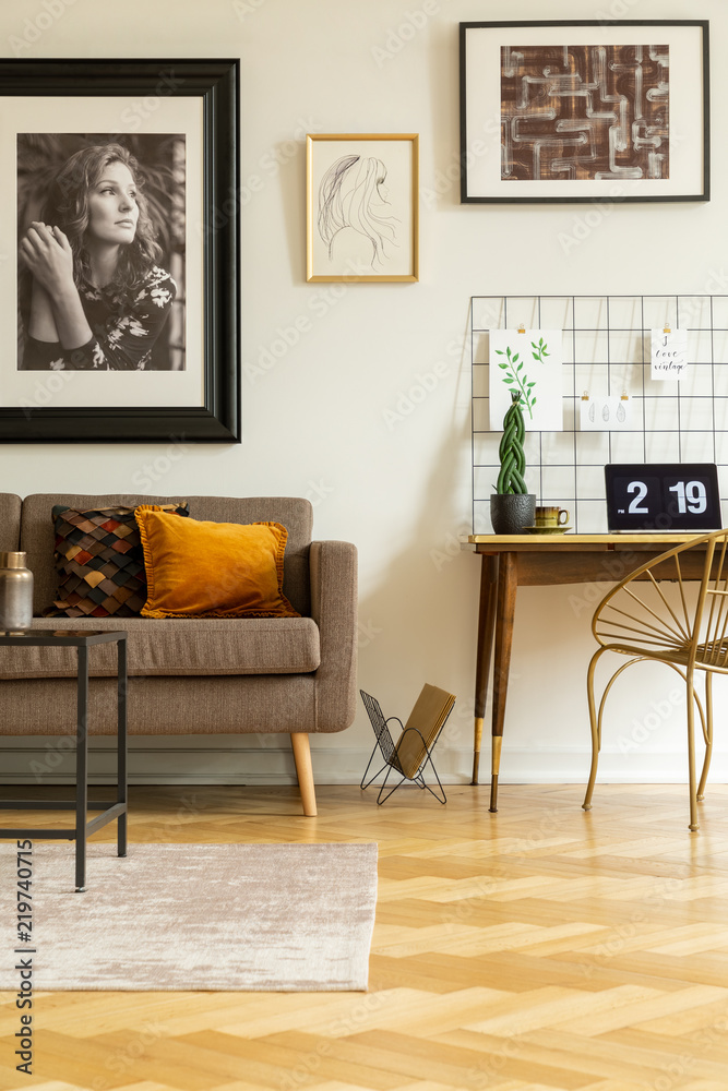 Posters above sofa next to chair and desk with laptop and plant in ...
