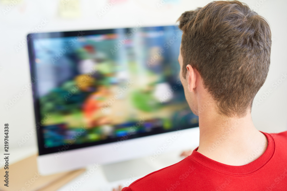 Back view of young designer in front of computer screen in moment of ...