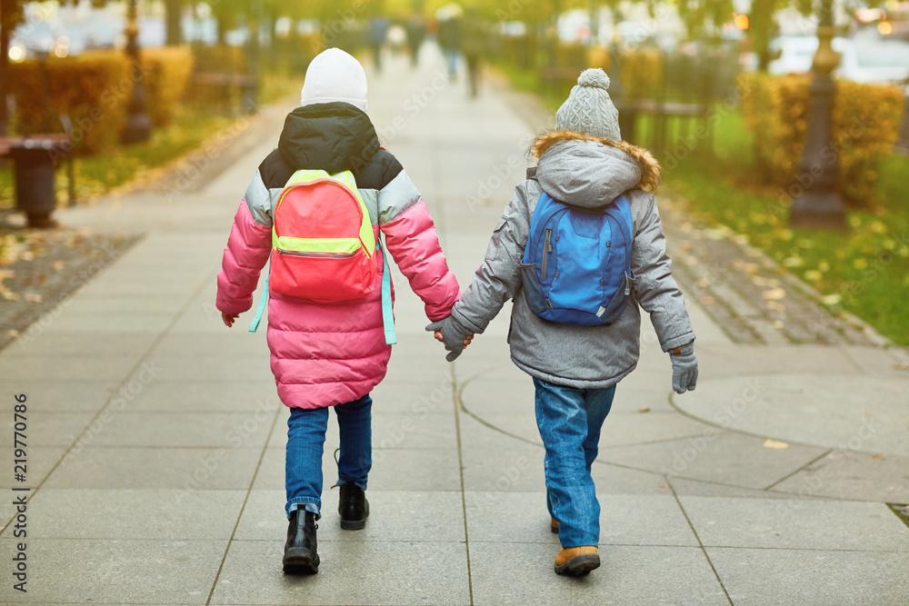 Back view of walking kids moving down trottoire in park with lawns and ...