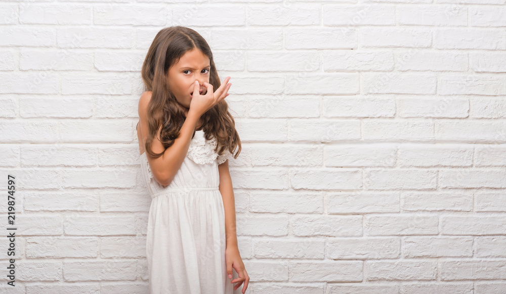 Young hispanic kid over white brick wall smelling something stinky and ...