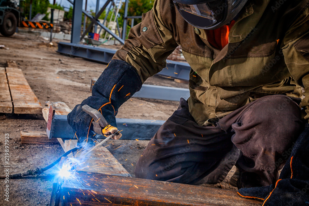 A strong man is a welder in brown uniform, welding mask and welders ...
