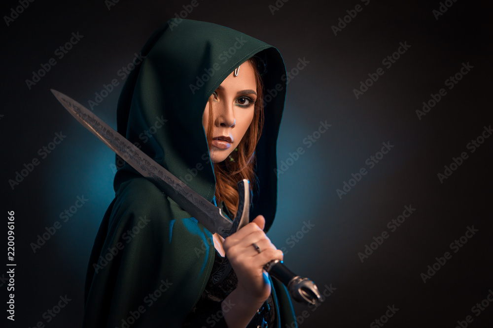 Mysterious young woman keeping sharp knife, wearing green cape with a ...