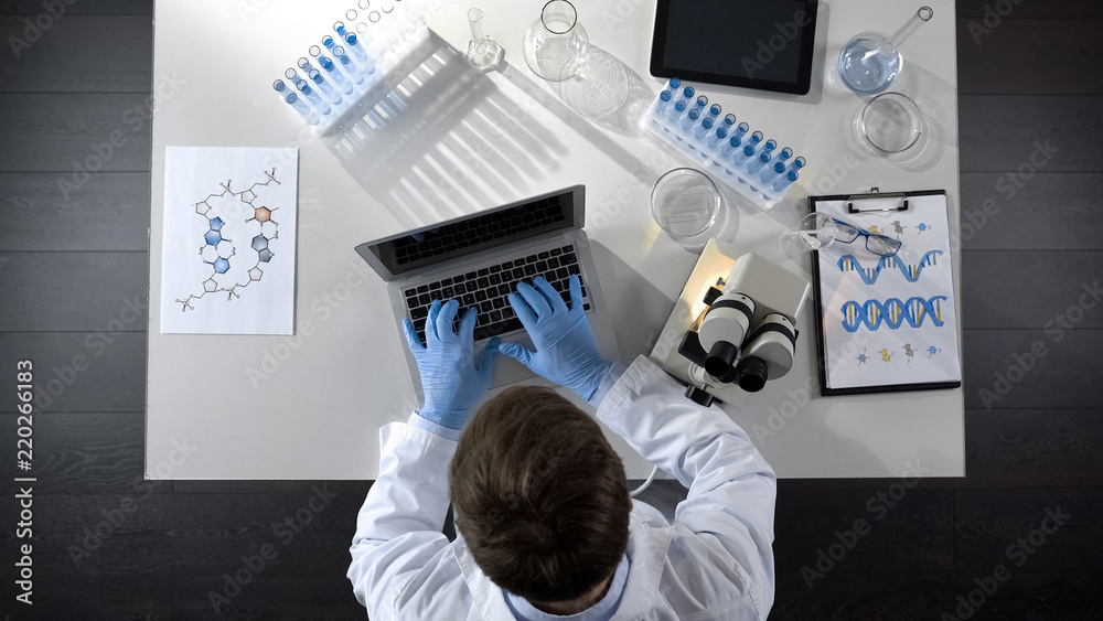 Lab worker viewing samples under microscope and typing results on ...