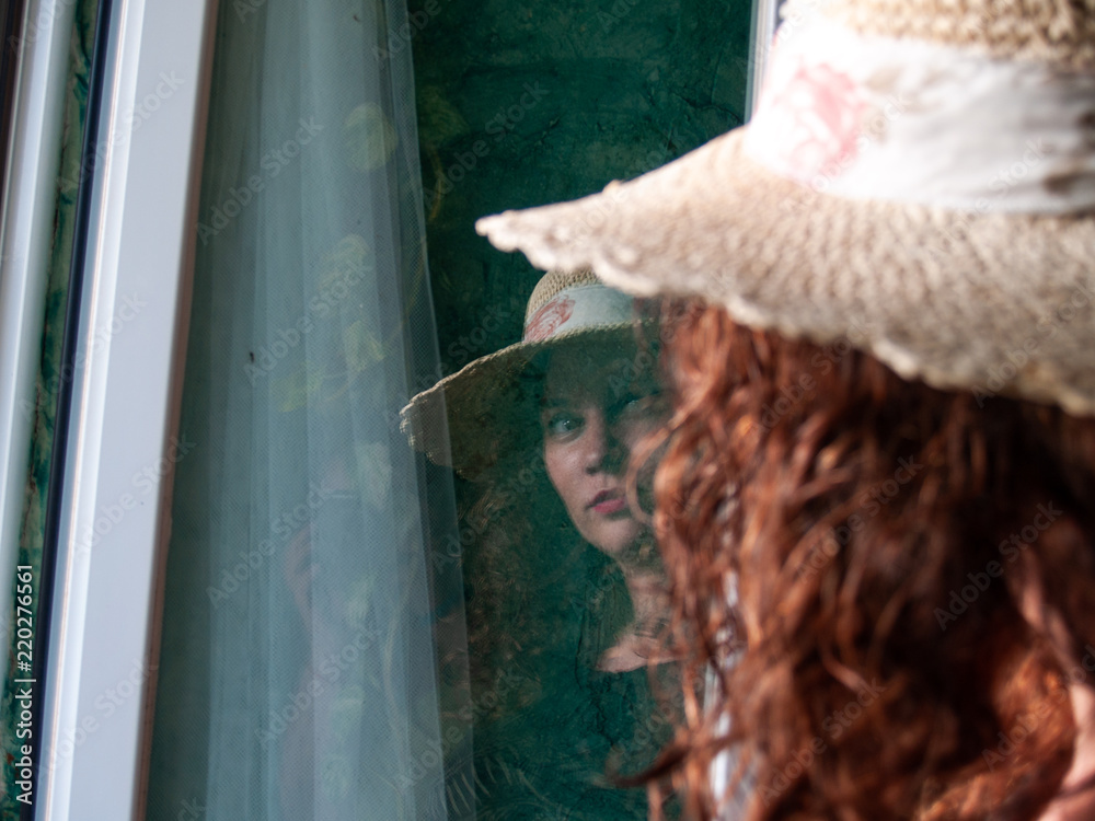 Reflection in a window of a young woman with curly hair wearing a straw ...